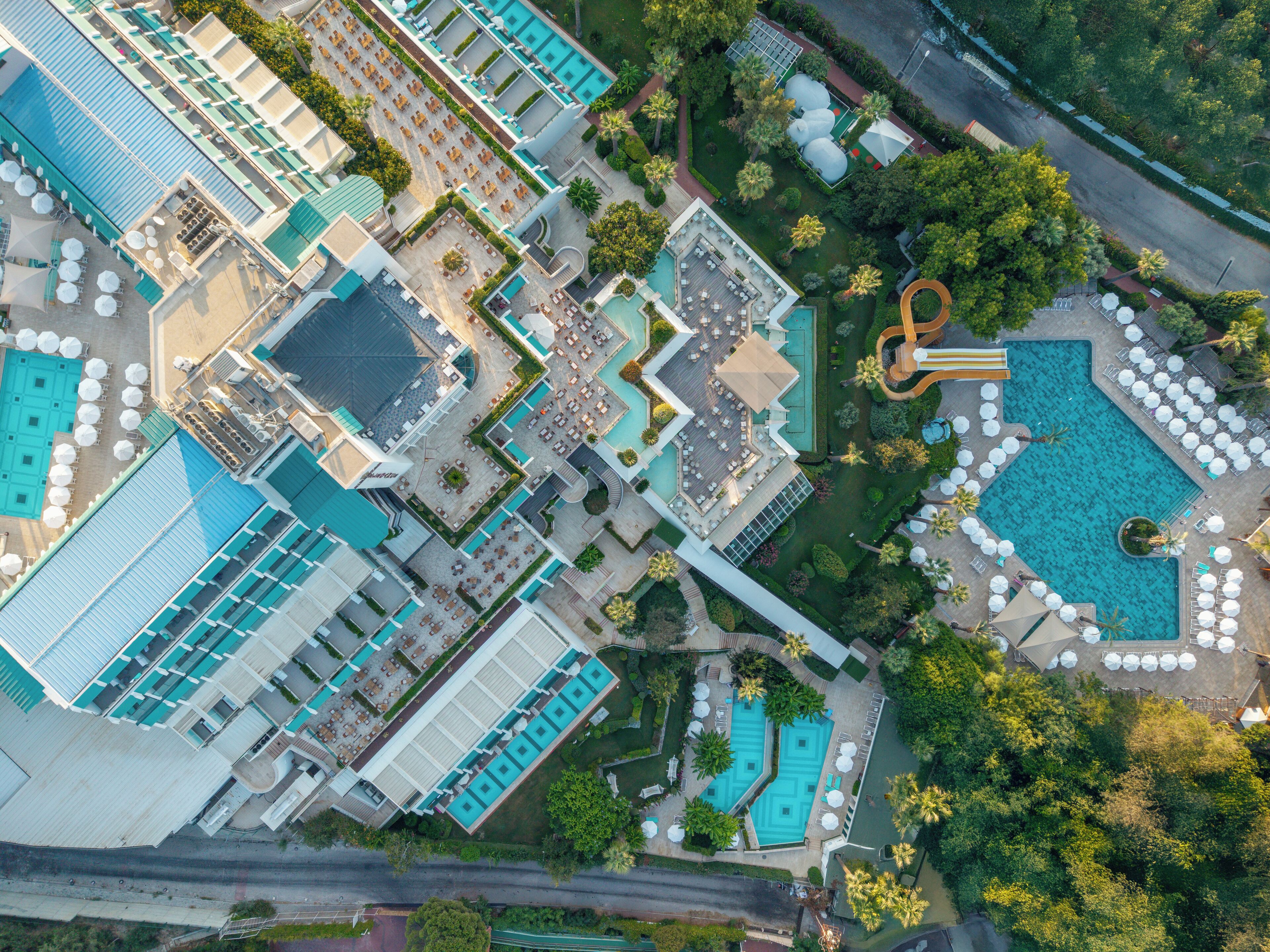 Vista aérea de um resort com várias piscinas, espreguiçadeiras e um grande tobogã.