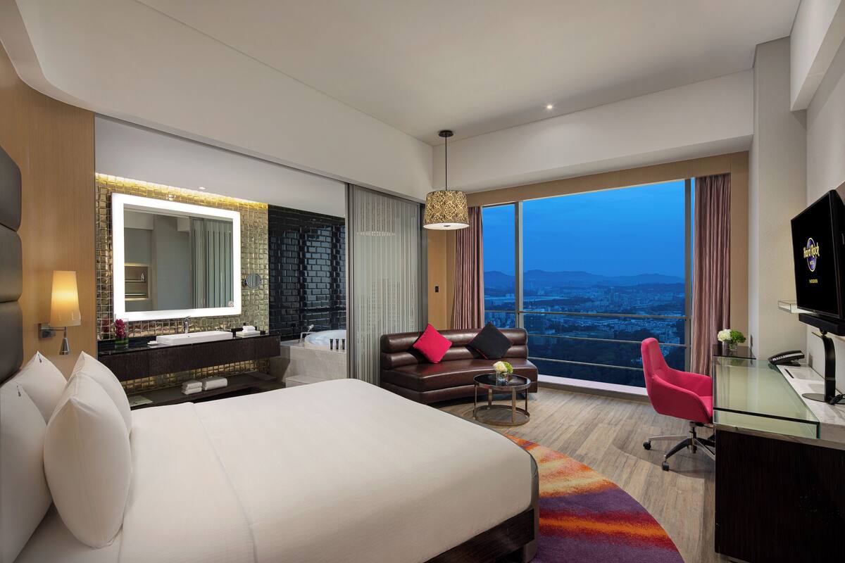 Quarto de hotel moderno com uma cama grande, um sofá, uma escrivaninha e uma televisão.