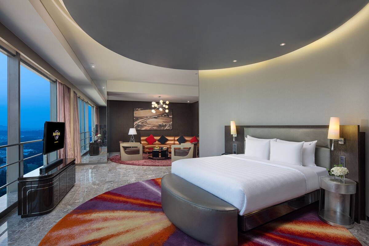Quarto de hotel moderno com uma cama grande, um sofá, uma televisão e vista para a cidade.