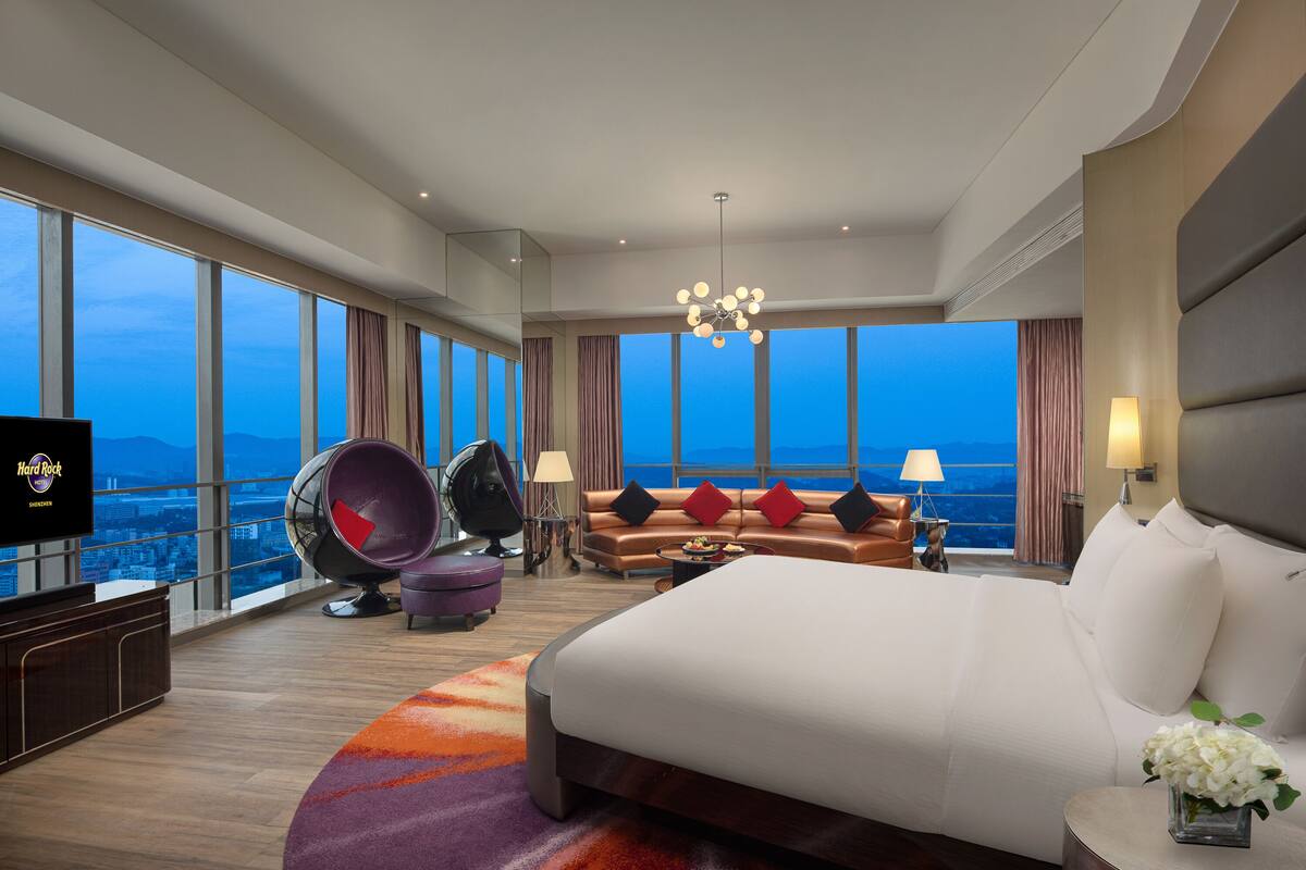 Quarto de hotel moderno com uma cama grande, um sofá, uma TV e vista para a cidade.