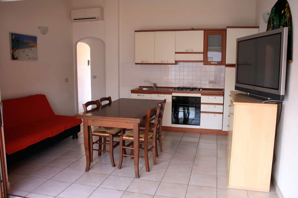 Uma cozinha compacta com uma mesa de jantar, cadeiras, um sofá vermelho e uma TV sobre um móvel.