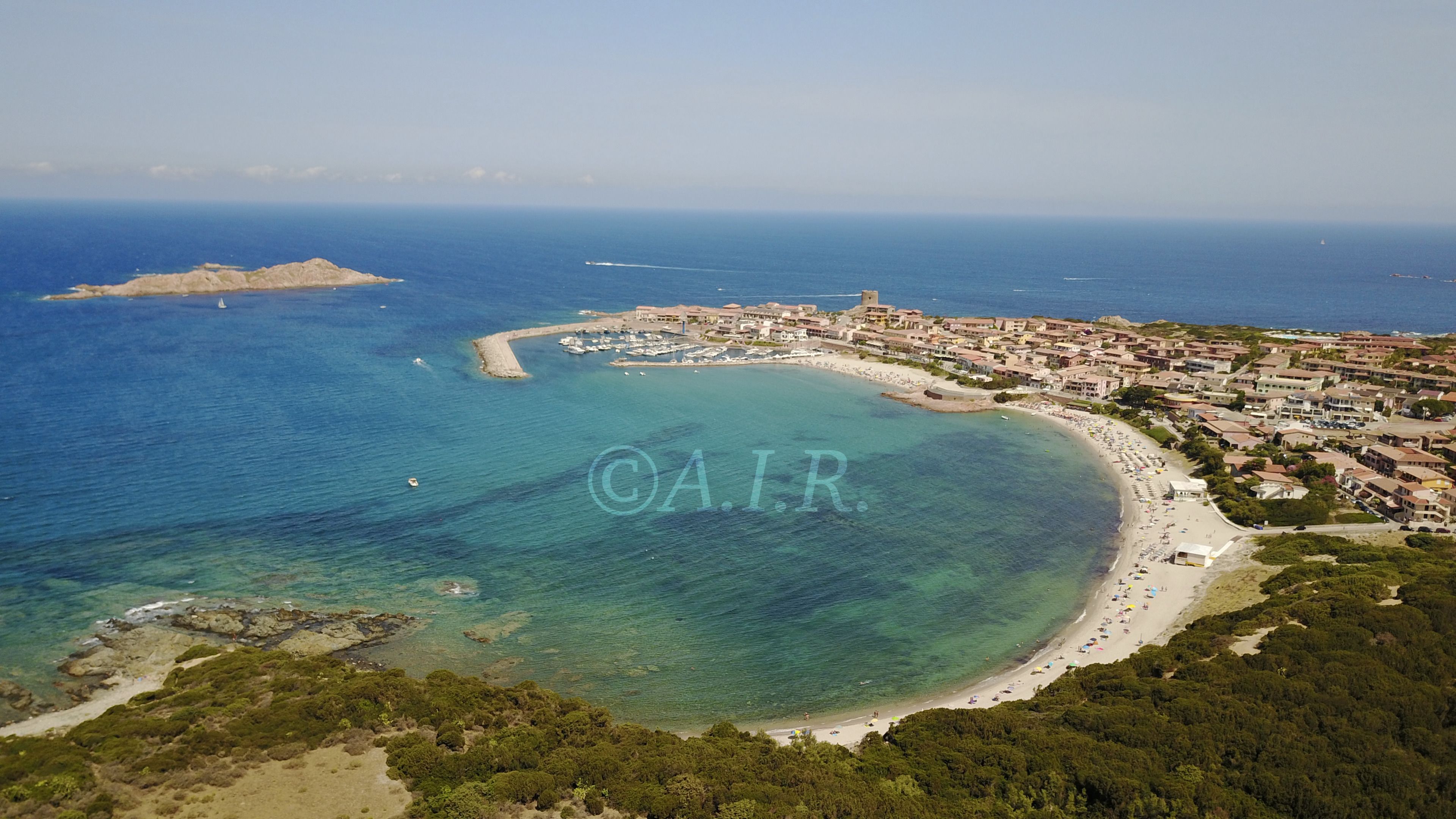 Vista aérea de uma cidade costeira com uma baía límpida, praias de areia e um porto de iates.