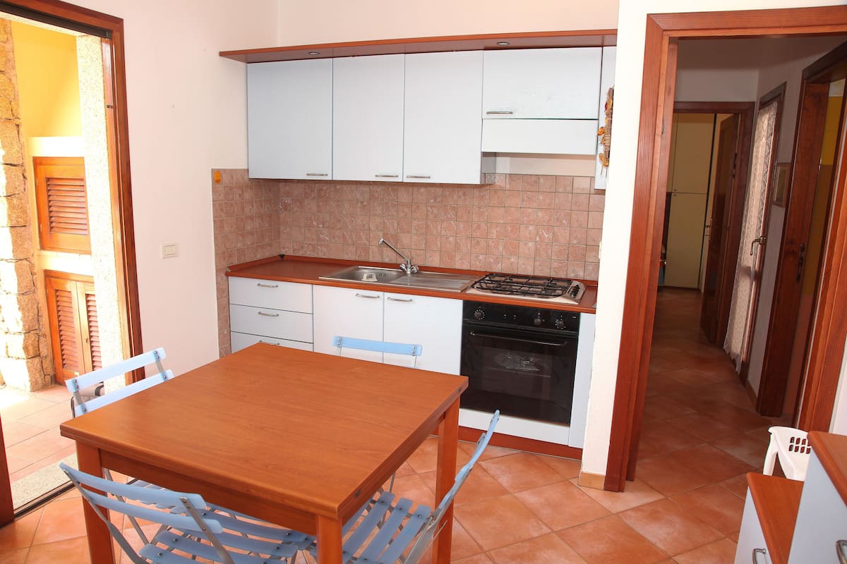 Uma cozinha compacta com armários brancos, uma mesa de madeira e cadeiras azuis.