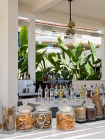 Uma área de bar com vista para um edifício com varandas, uma máquina de café e diversos frascos e potes com lanches.