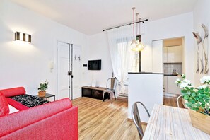 Uma sala de estar moderna com um sofá vermelho, uma mesa de jantar de madeira e uma cozinha ao fundo.