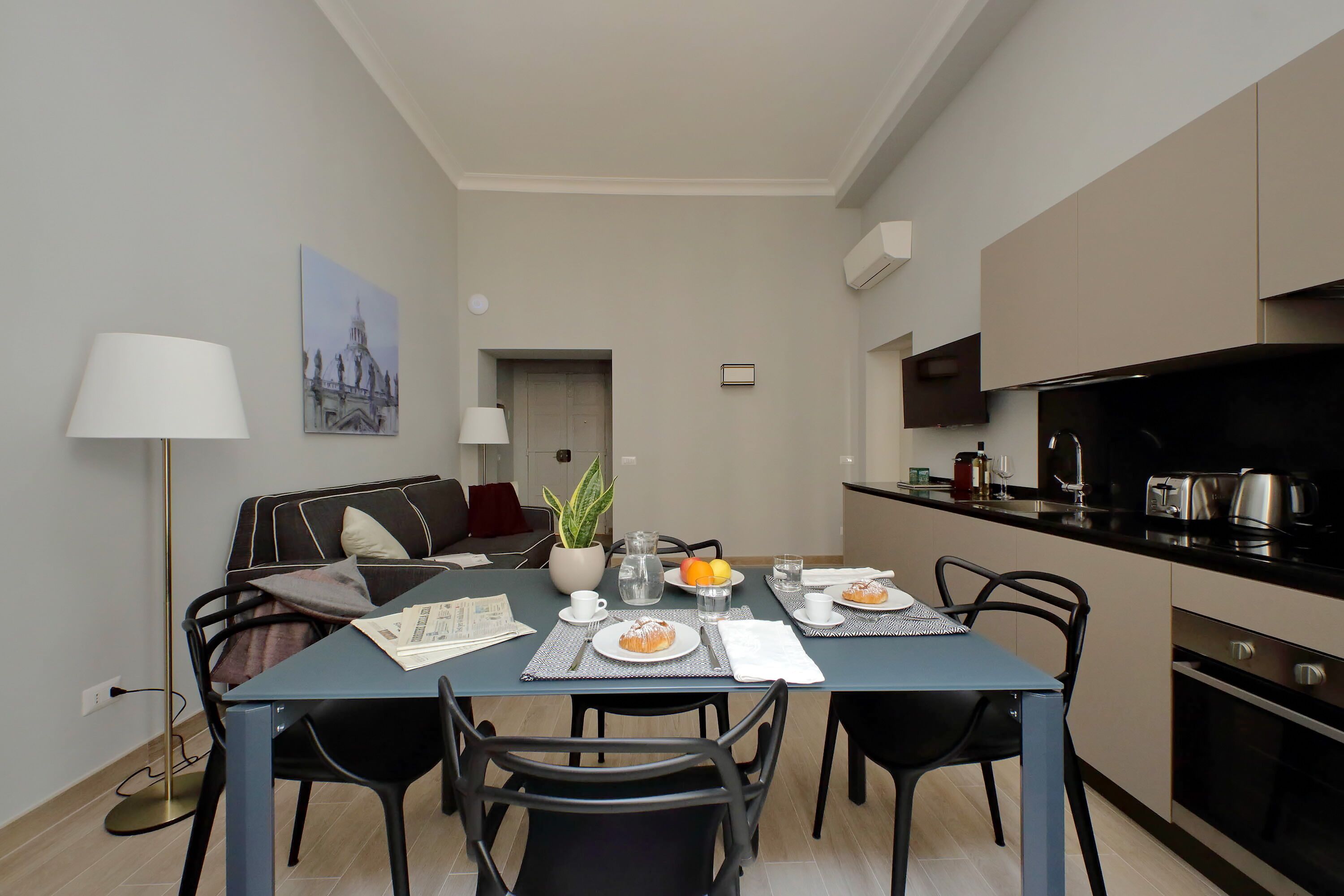 Uma sala de jantar moderna com uma mesa posta para dois, um sofá e uma cozinha com fogão e forno.