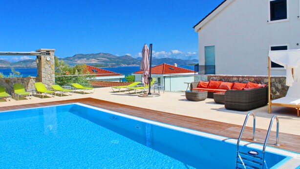Piscina com vista para o mar, um edifício branco e área de estar ao ar livre.
