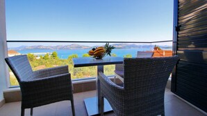 Varanda com cadeiras de vime e uma mesa, com vista para uma paisagem cênica de montanhas e um corpo de água.
