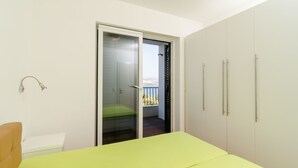 Quarto com cama, porta de correr de vidro que dá para uma varanda e um guarda-roupa.