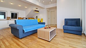 Uma sala de estar moderna com um sofá azul, uma mesa de centro de madeira e uma cozinha ao fundo.