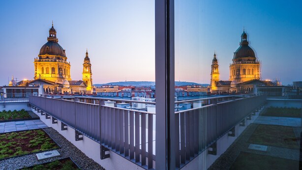 Um edifício moderno com fachada de vidro e um jardim no terraço.