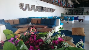 Ampla sala de estar com sofá azul, mesa de centro de madeira e um painel decorativo com a palavra "JUJUTURI".