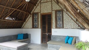 Quarto com teto inclinado, porta de madeira e duas áreas de estar com almofadas.