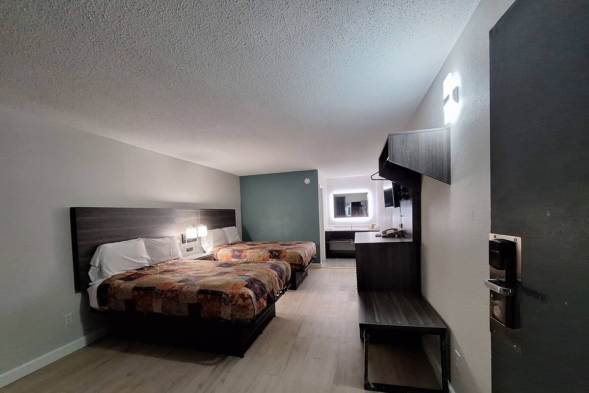 Quarto de hotel com duas camas, uma escrivaninha, um espelho e uma pequena área de estar.