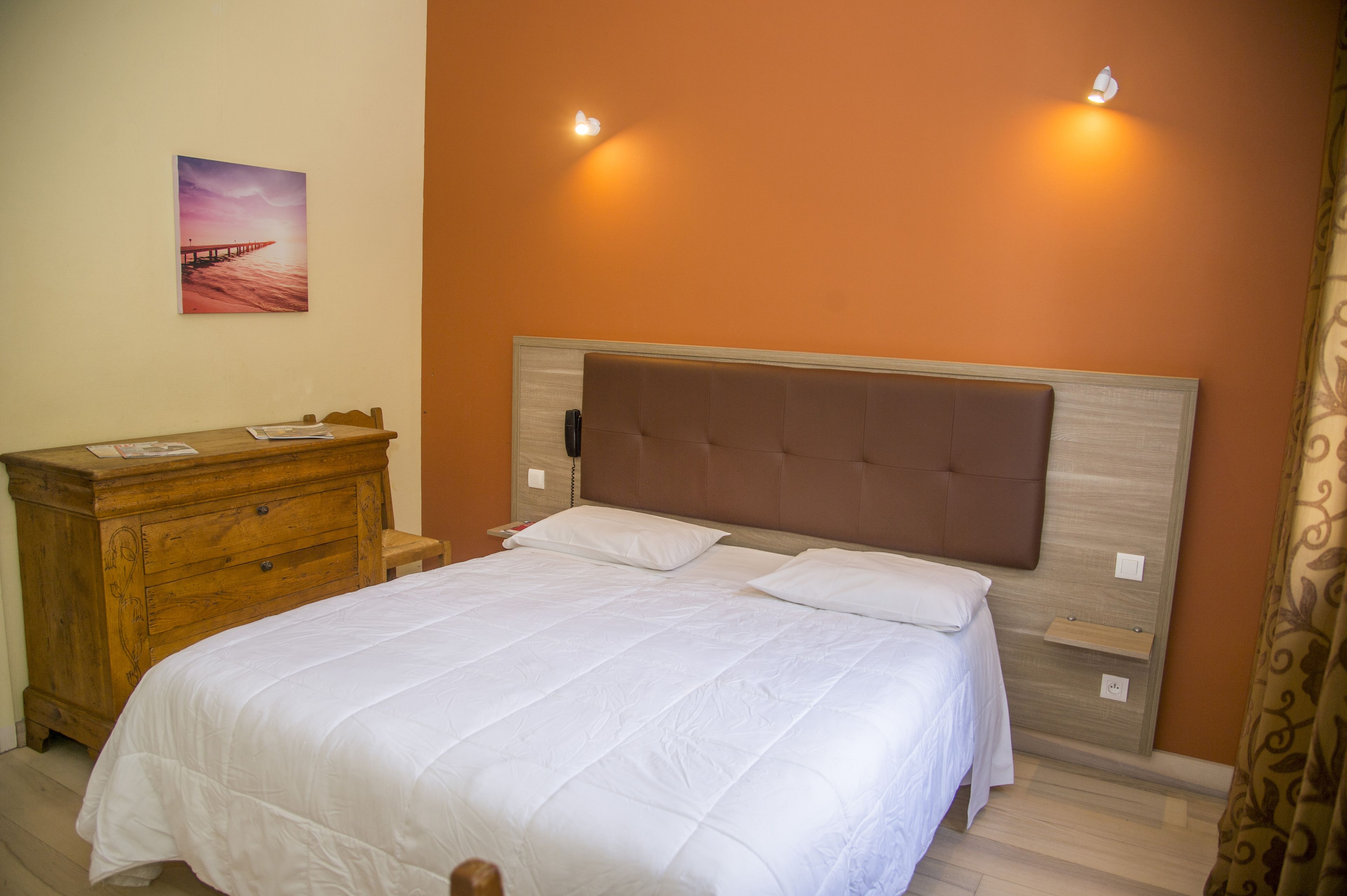 Quarto com uma cama grande, cômoda de madeira e um quadro na parede.