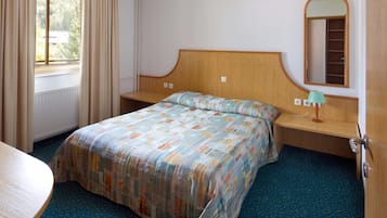 Quarto de hotel com cama, mesa de cabeceira, abajur, espelho e janela com cortinas.