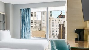 Quarto de hotel com uma cama grande, uma escrivaninha e vista para edifícios da cidade.