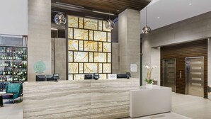 Uma área de recepção de hotel com um balcão de mármore, um minibar e um espaço de estar com cadeiras azul-turquesa.