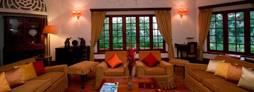 Quarto com sofá, mesa com um vaso e armário. Há janelas com cortinas e arandelas.