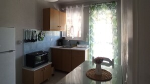 Cozinha compacta com geladeira, micro-ondas e armários de madeira. Há uma mesa de jantar com cadeiras e uma janela com cortinas.