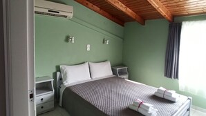 Um quarto com teto de madeira, uma cama com colcha acolchoada, duas mesas de cabeceira e um ar condicionado fixado na parede.