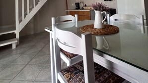 Uma cozinha moderna com armários brancos, uma geladeira branca e uma área de jantar com mesa de vidro e cadeiras brancas.