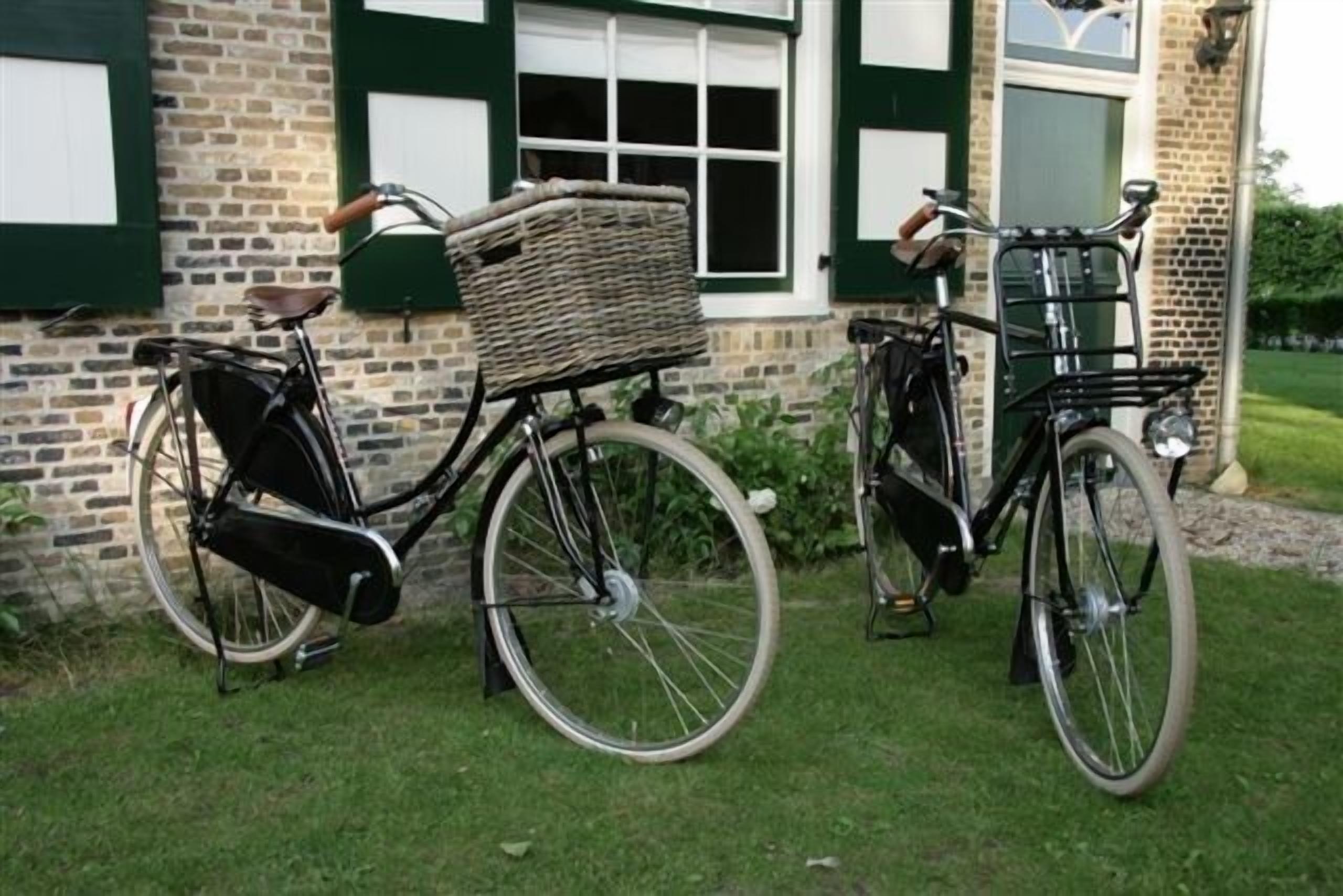 Duas bicicletas estacionadas em frente a um edifício de tijolos com persianas verdes.
