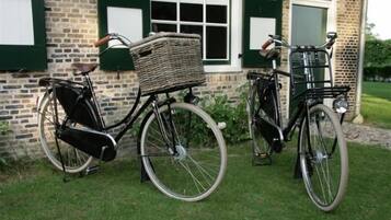 Duas bicicletas estacionadas em frente a um edifício de tijolos com persianas verdes.