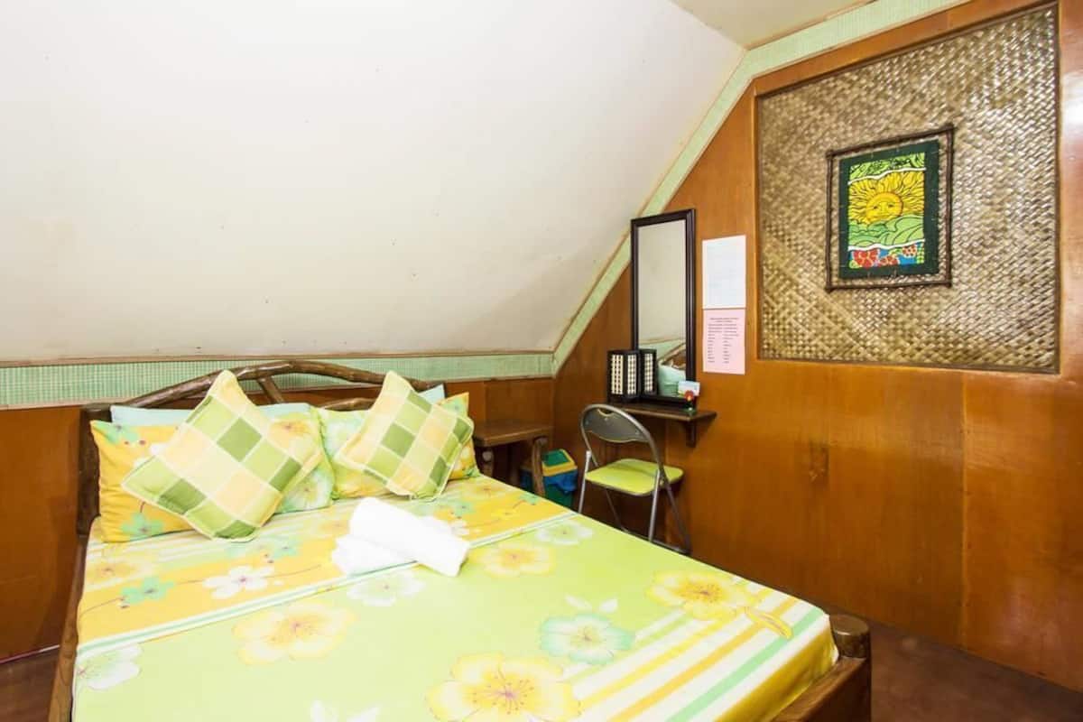 Quarto com cama, cadeira, escrivaninha com computador e quadro pendurado na parede.
