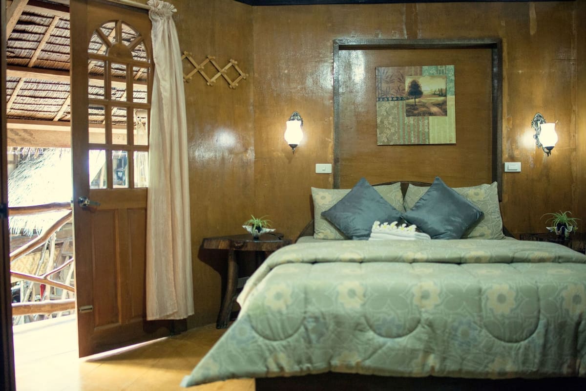 Quarto com cama, mesas de cabeceira, luminária na parede, porta e janela.
