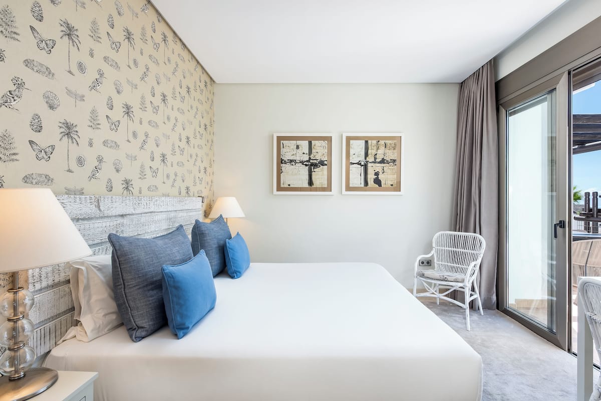 Quarto de hotel com uma cama grande, uma cadeira branca e duas obras de arte emolduradas na parede.