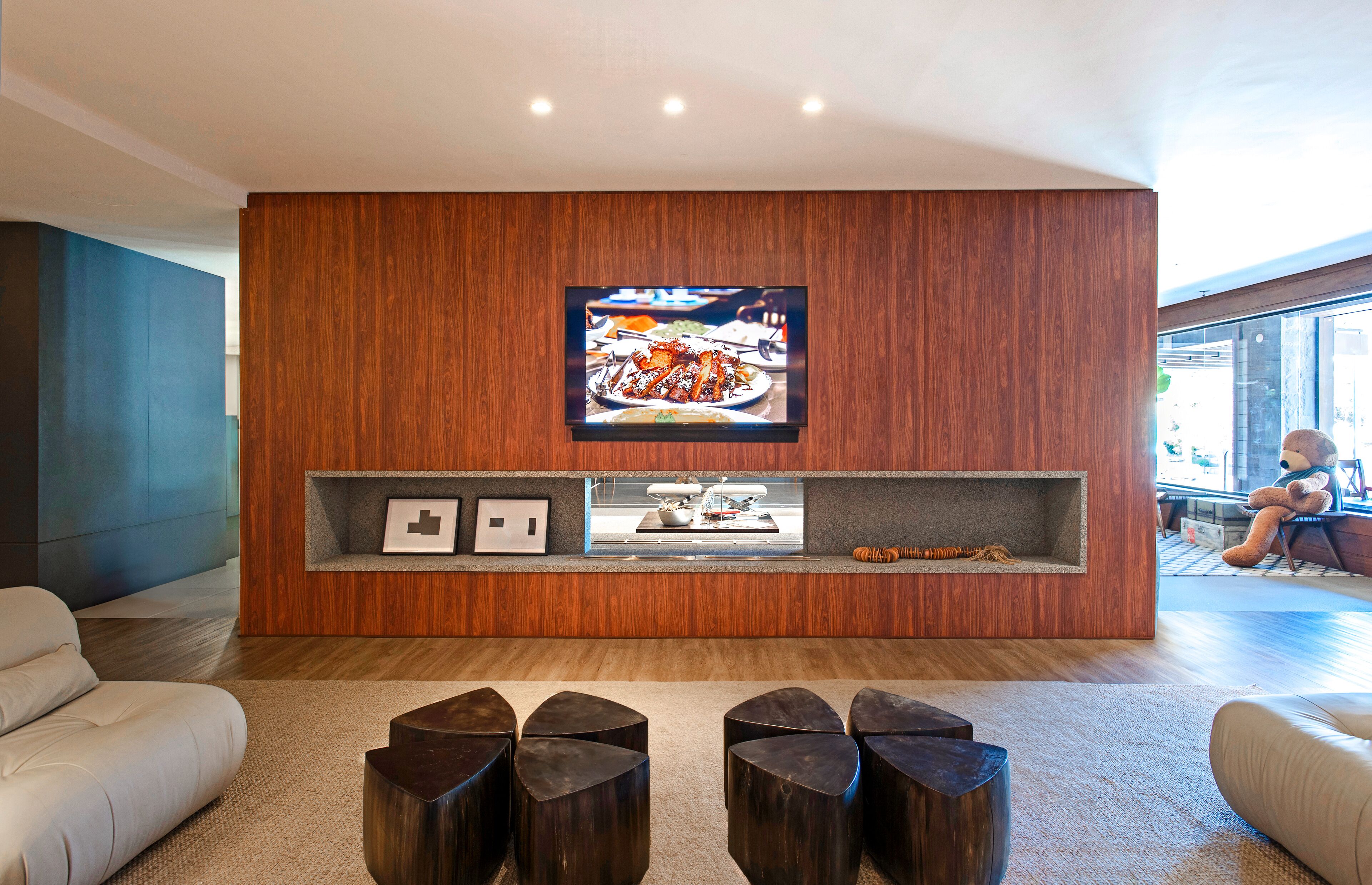 Uma sala de estar moderna com uma parede em madeira, uma televisão de tela plana e uma estante embutida com objetos decorativos.