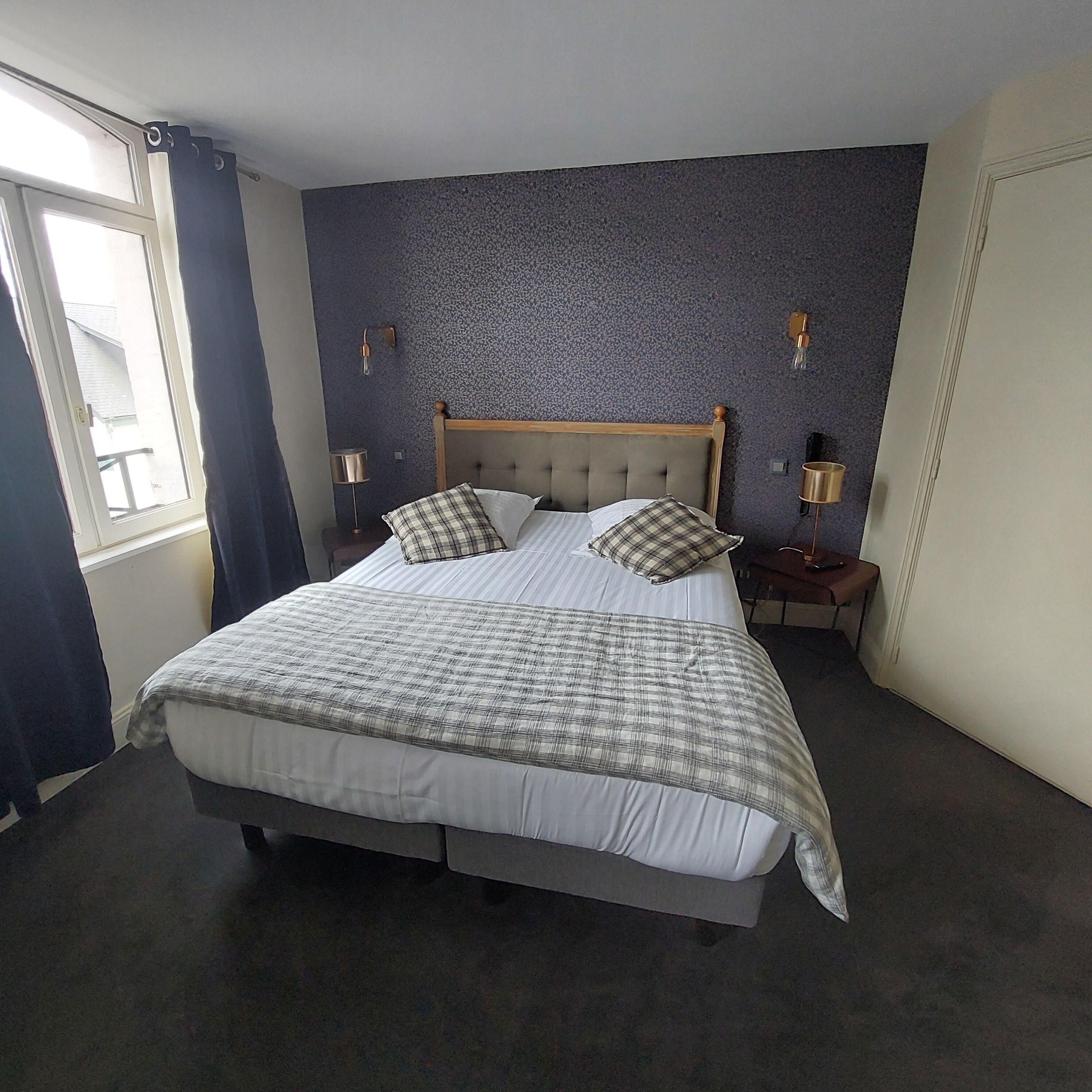 Cama bem arrumada com colcha xadrez e duas almofadas, cabeceira de madeira e duas luminárias de cabeceira.