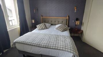 Cama bem arrumada com colcha xadrez e duas almofadas, cabeceira de madeira e duas luminárias de cabeceira.