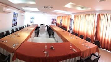 Uma sala de conferências com mesas grandes, cadeiras e um amplo janelão com cortinas.