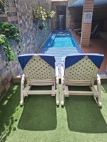 Área de piscina com duas espreguiçadeiras, um muro de pedra e uma cascata.