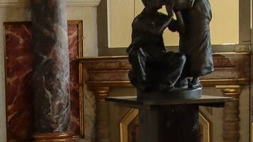 Uma estátua de um homem e uma criança em um salão com colunas de mármore e lareira.