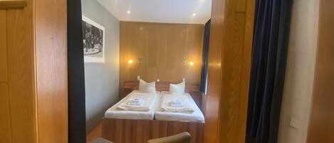 Quarto de hotel com duas camas, teto de madeira e uma pequena mesa.