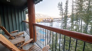 Uma varanda com cadeiras de madeira e vista para um resort de montanha com piscina.