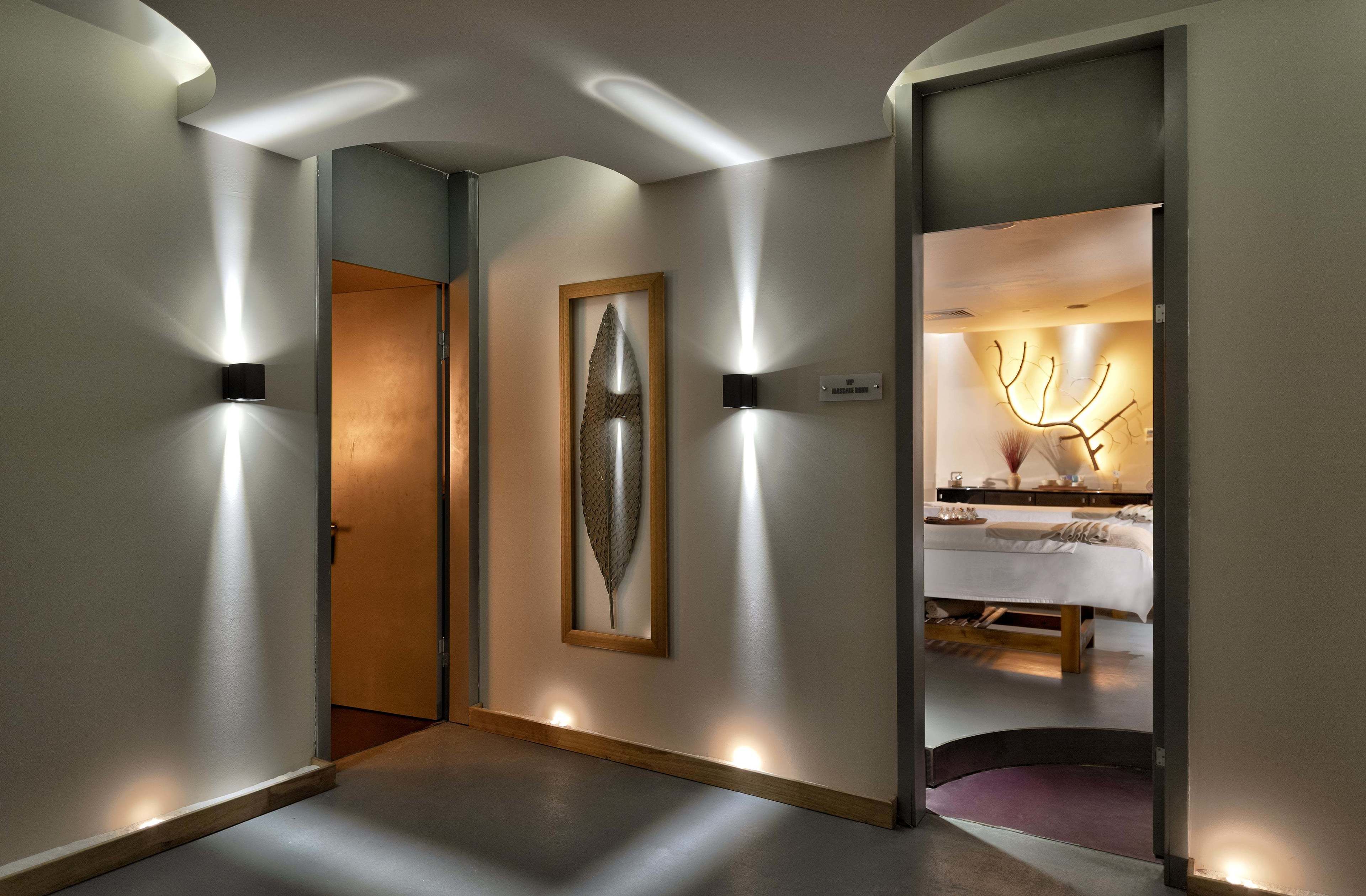 Um corredor com uma cama, uma obra de arte com penas emoldurada e luminárias fixadas na parede.
