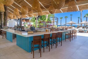 Uma área de bar com balcão, banquetas e luminárias de vime pendentes.