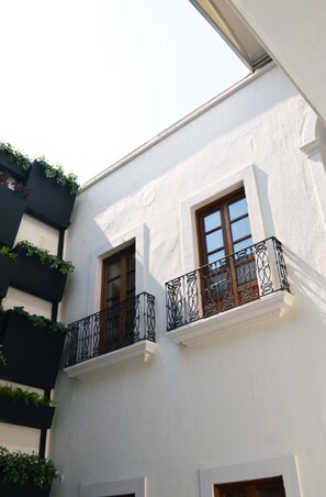 Um edifício com paredes brancas, duas janelas com molduras de madeira e uma varanda com grades de ferro forjado.