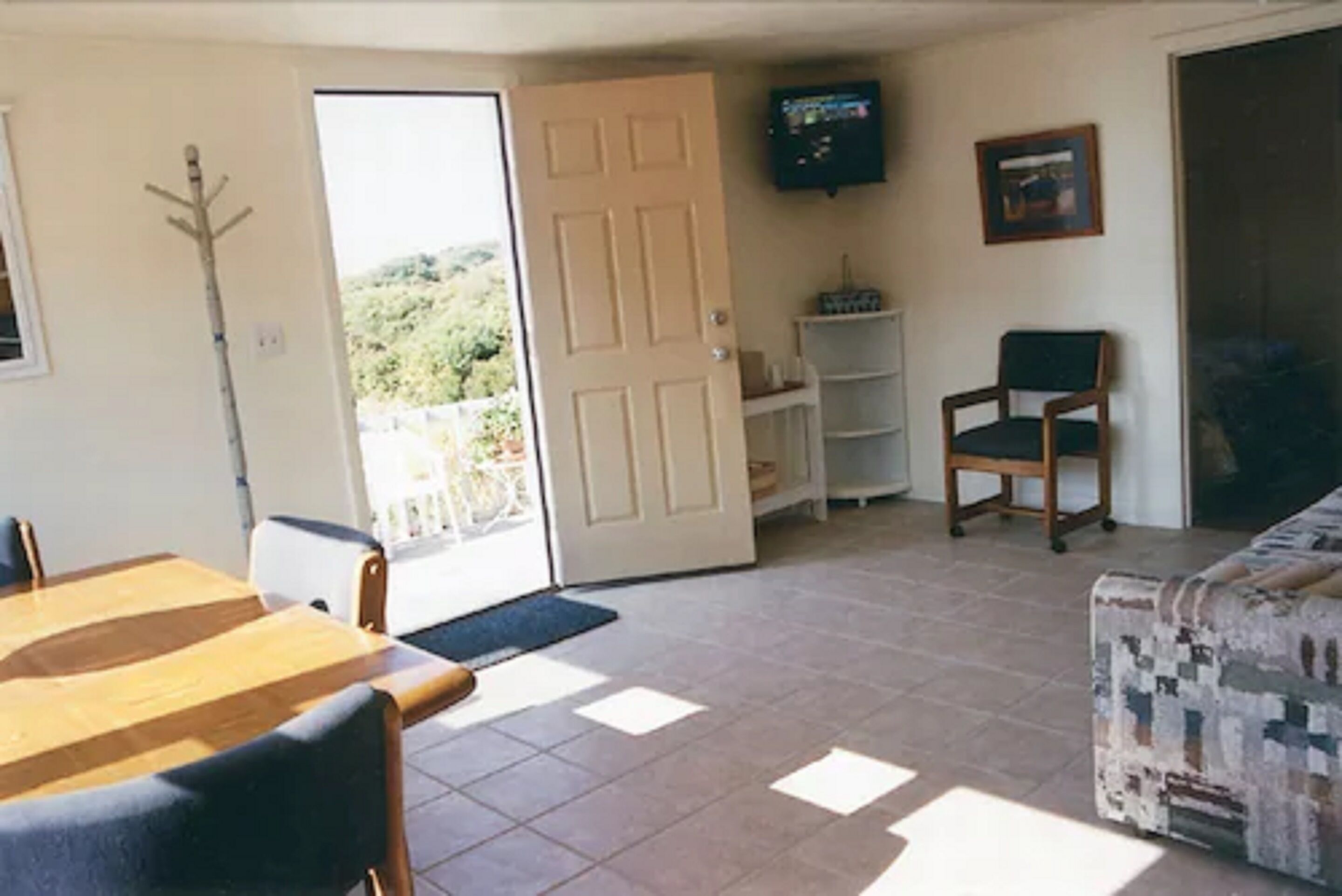 Quarto com mesa de jantar e cadeiras, um sofá, televisão e porta que dá para o exterior.