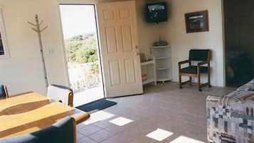 Quarto com mesa de jantar e cadeiras, um sofá, televisão e porta que dá para o exterior.