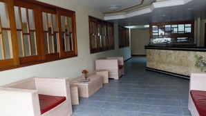 Um hall com móveis de vime, um balcão de recepção e piso de azulejos.