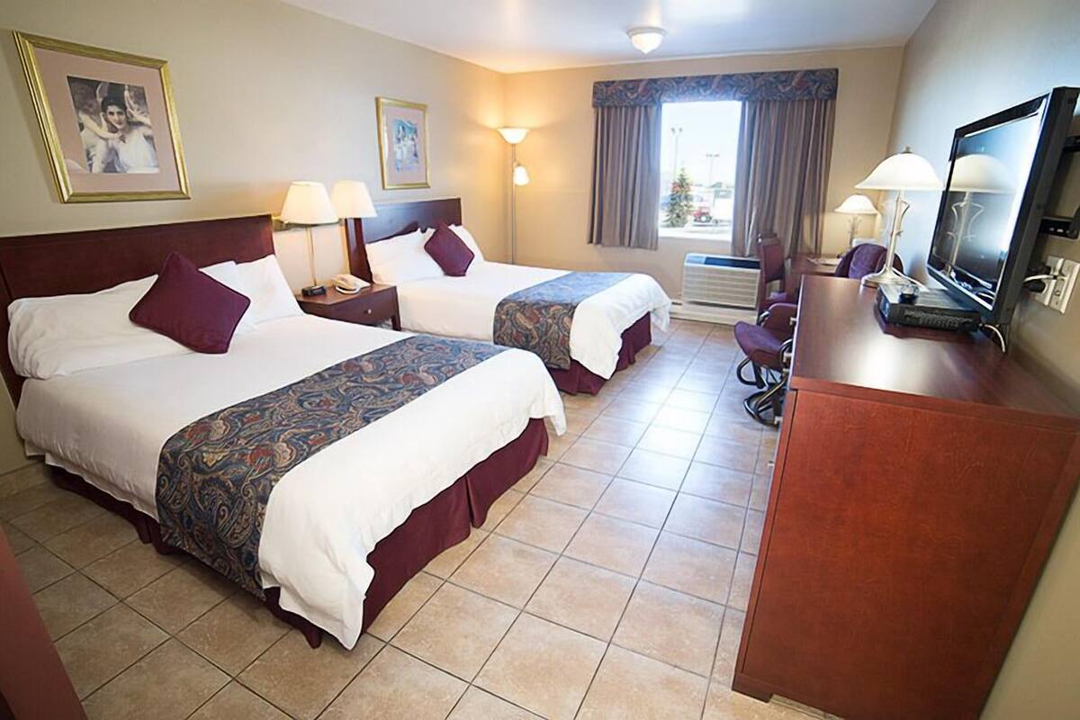 Quarto de hotel com duas camas, uma escrivaninha, televisão e janela com cortinas.