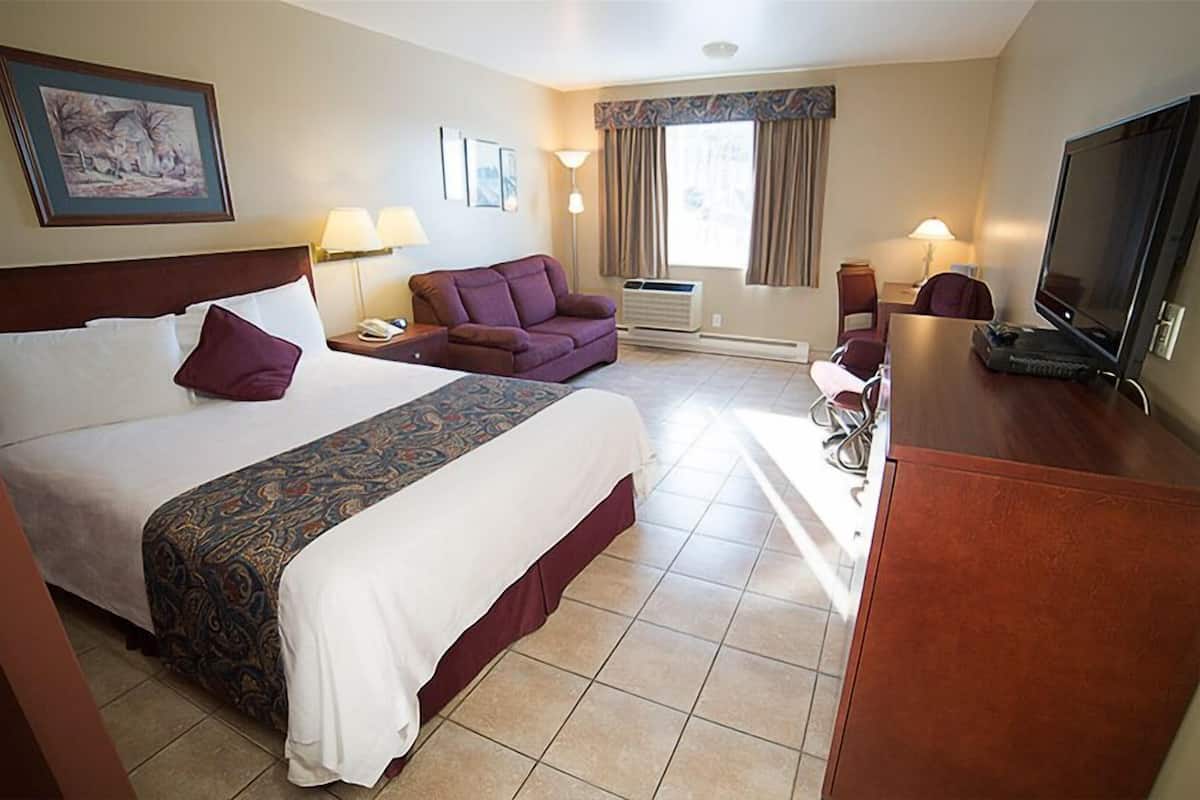 Quarto de hotel com uma cama grande, um sofá, uma escrivaninha com televisão e uma janela com cortinas.