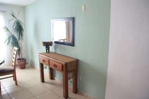 Quarto com mesa de consola de madeira, uma cadeira, planta em vaso e um espelho na parede.