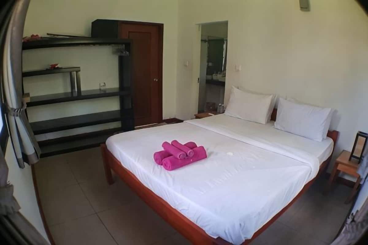 Quarto de hotel com uma cama, mesa de cabeceira de madeira, um espelho e um guarda-roupa.