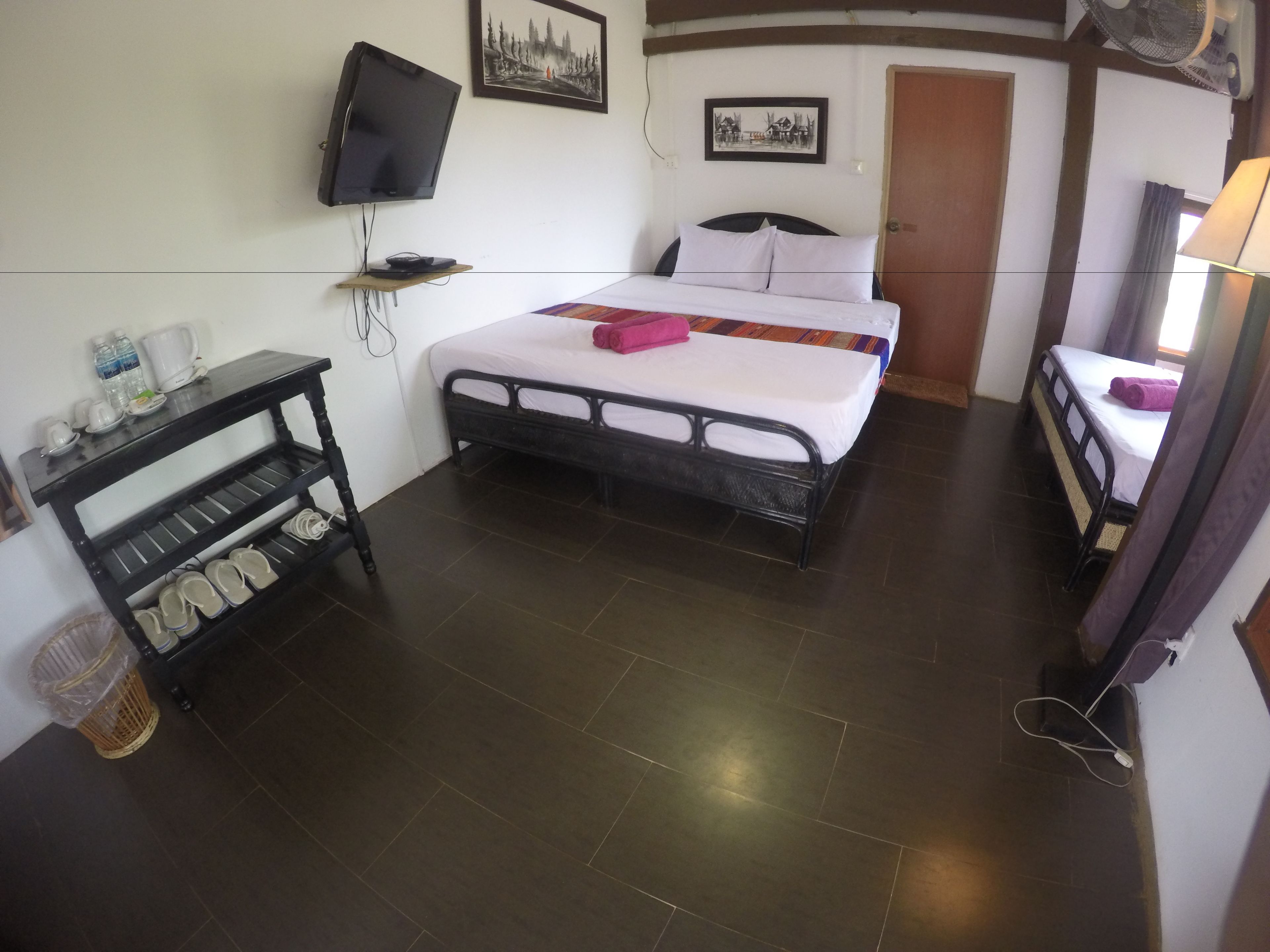 Quarto com cama, televisão na parede, mesinha com prateleira e uma porta.